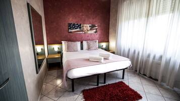 Quarto com cama, tapete vermelho, pintura da bandeira americana e janela com cortinas.