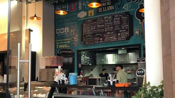 Interior de café com quadro de menu, balcão com funcionários e vitrine de vidro.