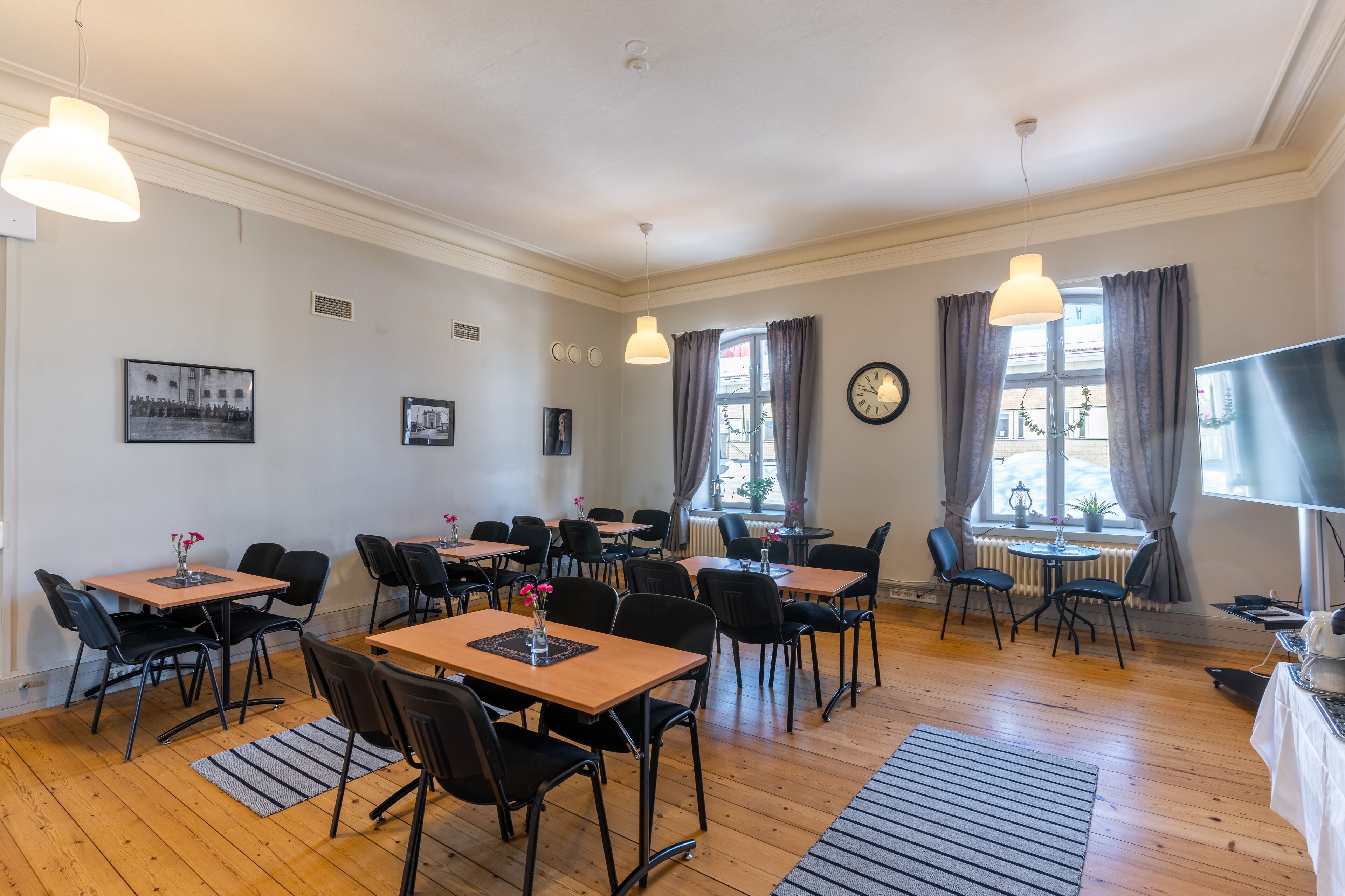 Uma sala de jantar com várias mesas e cadeiras, um relógio na parede e uma televisão sobre uma mesa.