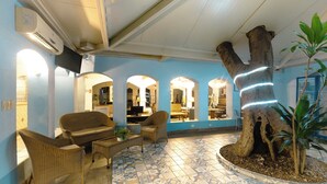 Um hall com móveis de vime, piso de azulejos e uma escultura de árvore central.