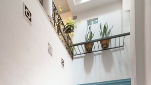 Interior com vários níveis, piso de azulejos, escada com corrimão e uma pessoa caminhando pelo corredor.