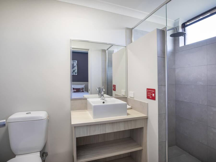 Uma casa de banho moderna com sanita branca, lavatório com espelho e zona de duche.
