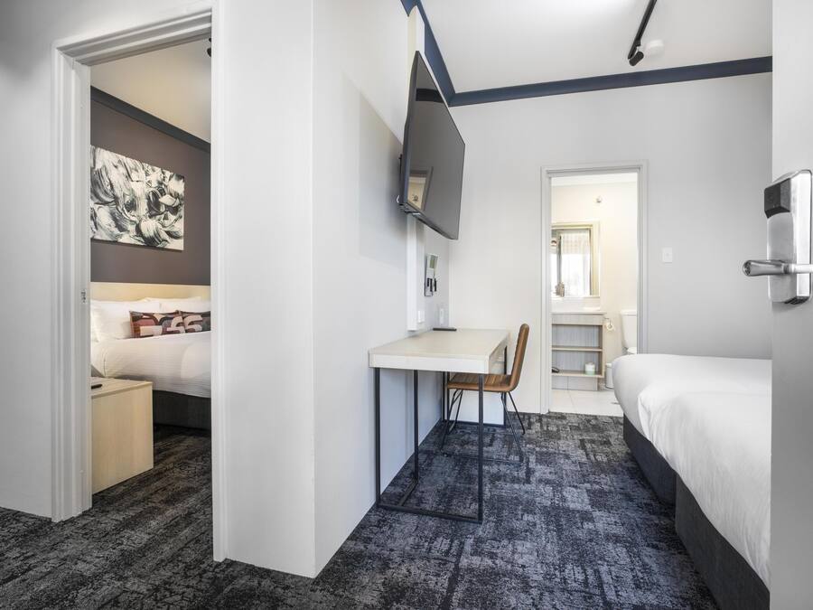 Quarto de hotel com cama, escrivaninha, cadeira, televisão de tela plana e um quadro na parede.