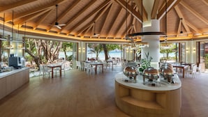 Um espaço amplo e interno, com vigas de madeira, uma ilha central com equipamentos de preparação de alimentos e grandes janelas com vista para o exterior.
