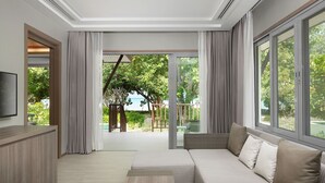 Uma sala de estar moderna com um sofá, uma mesa de centro e uma TV sobre um aparador de madeira. Grandes janelas oferecem vista para um jardim e uma piscina.
