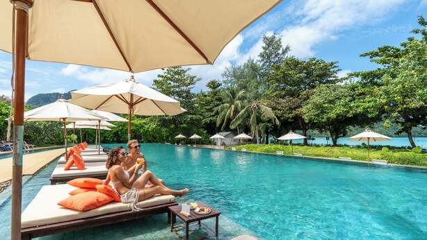 Área de piscina com espreguiçadeiras, guarda-sóis e vista para o mar.