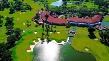 Vista aérea de um campo de golfe com clube, lagoas e vegetação ao redor.