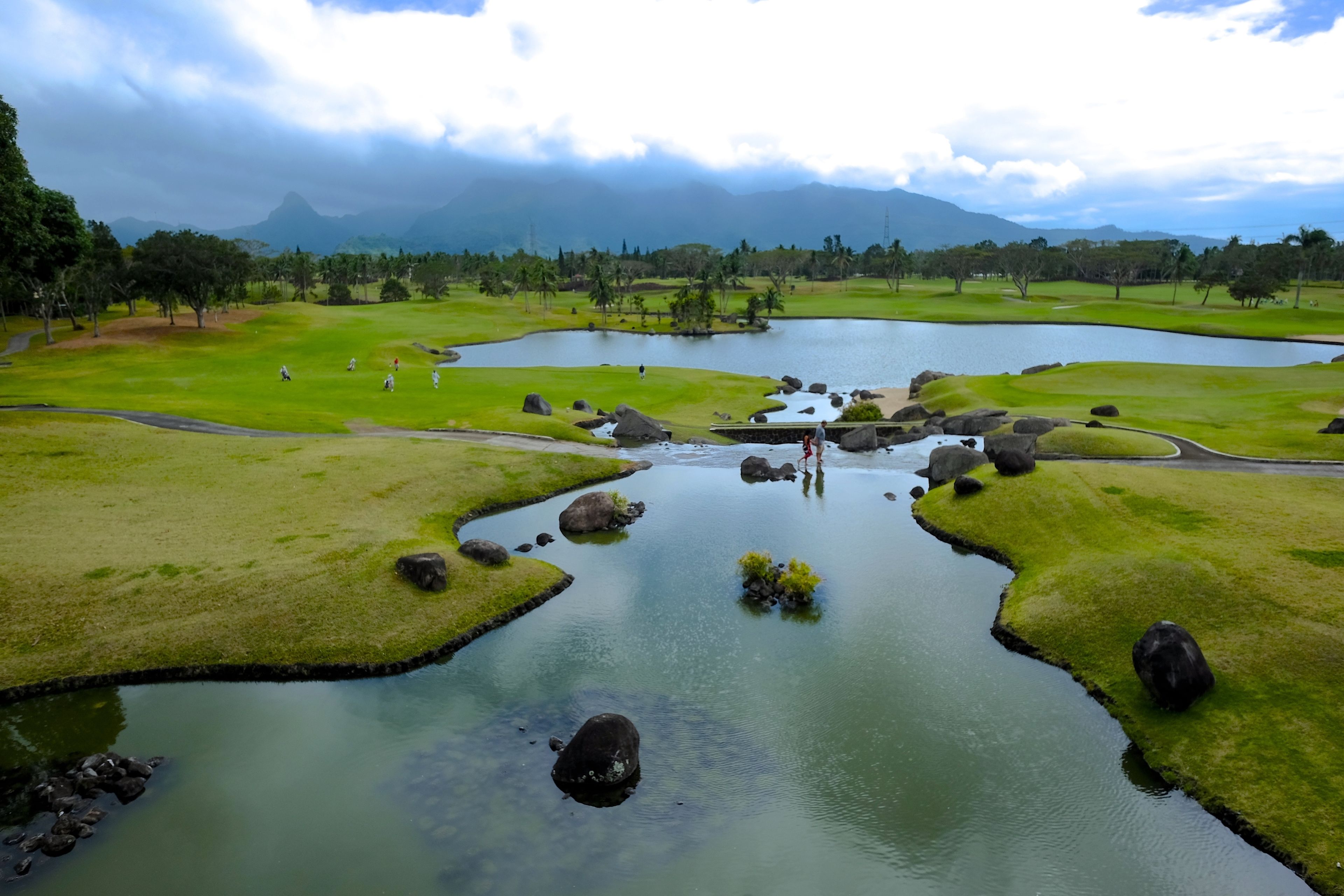 Um campo de golfe com várias lagoas e montanhas ao fundo.