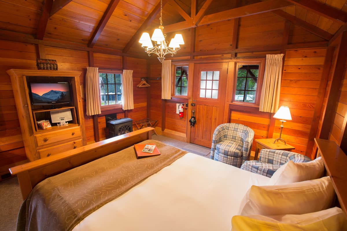 Quarto de cabana de madeira com uma cama, televisão, escrivaninha e uma cadeira.