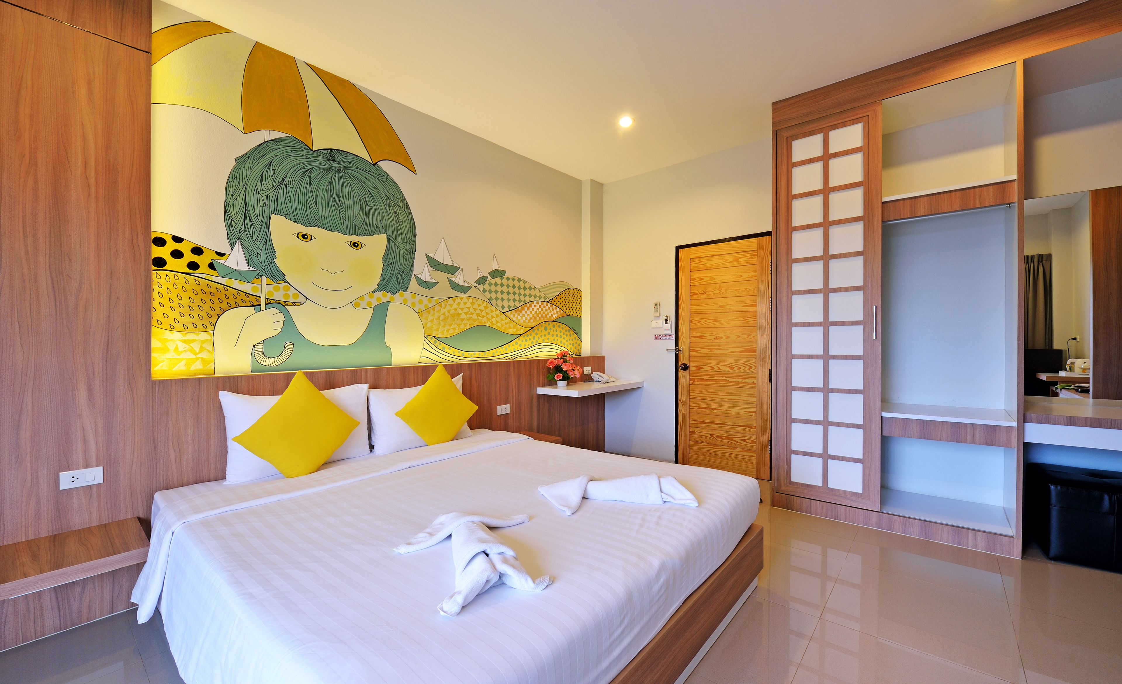 Quarto de hotel com uma cama grande, um guarda-roupa de madeira, uma pequena mesa de cabeceira com telefone, e um mural na parede.