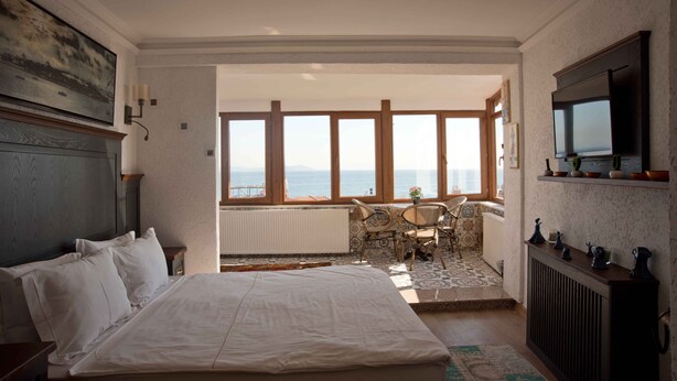 Quarto com uma cama grande, televisão e vista para o mar através de amplas janelas.