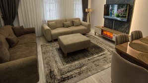 Uma sala de estar moderna com um sofá, um banquinho e uma TV fixada na parede.