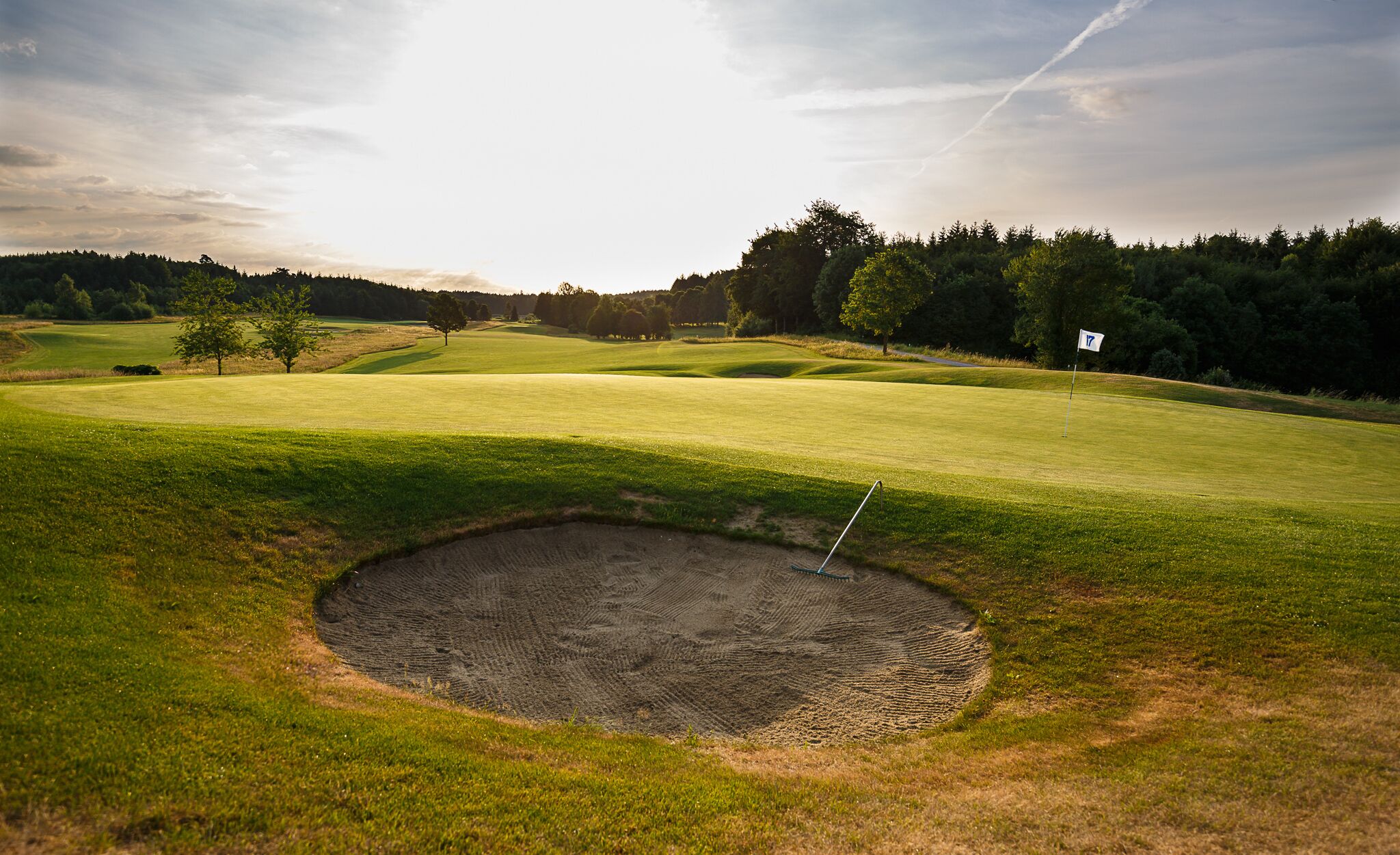 Um campo de golfe com um bunker de areia, haste de sinalização e bandeira indicando o buraco 17.