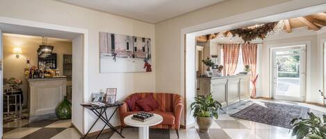 Uma sala de estar ampla com piso xadrez, um sofá, uma mesa pequena com revistas e um quadro na parede.