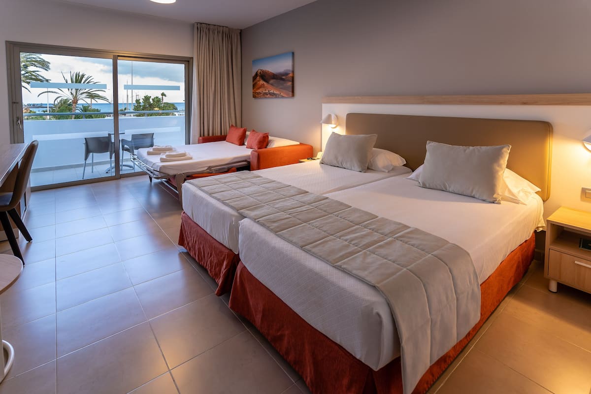 Quarto de hotel com uma cama grande, uma escrivaninha e uma varanda com vista para o mar.