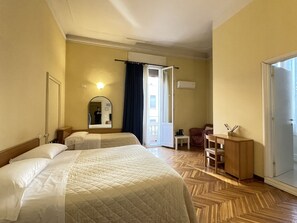 Quarto de hotel com duas camas, piso de madeira, uma mesa pequena, uma cadeira e um espelho.
