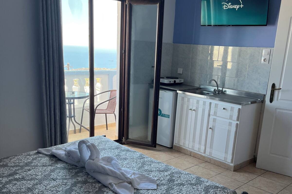 Quarto de hotel com cama, televisão, cozinha compacta e varanda com vista.