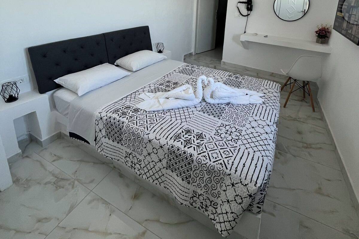 Quarto moderno com cama, mesas de cabeceira, escrivaninha, espelho e porta.