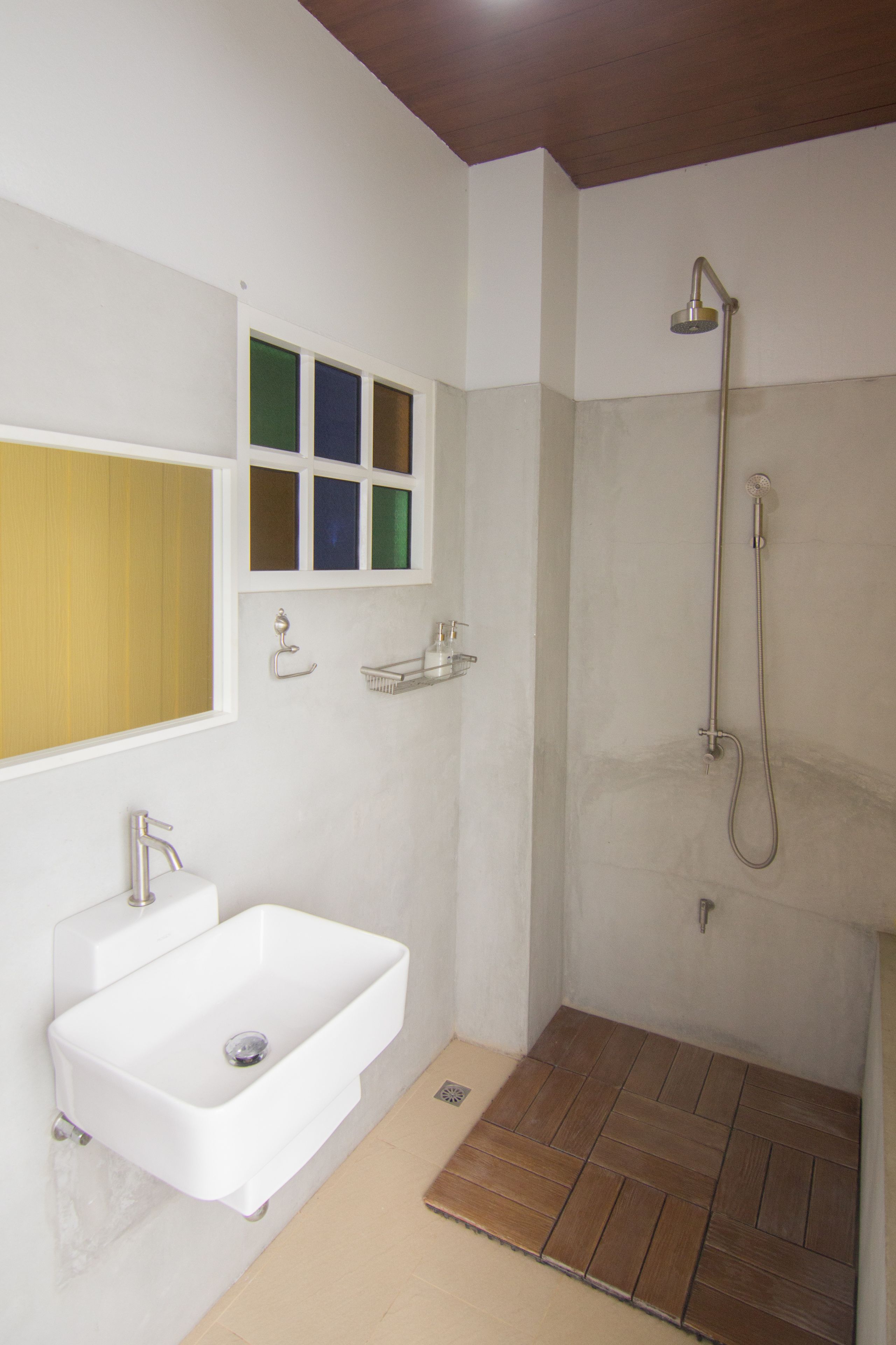 Casa de banho com lavatório branco, chuveiro com chuveiro de mão e espelho com moldura colorida.