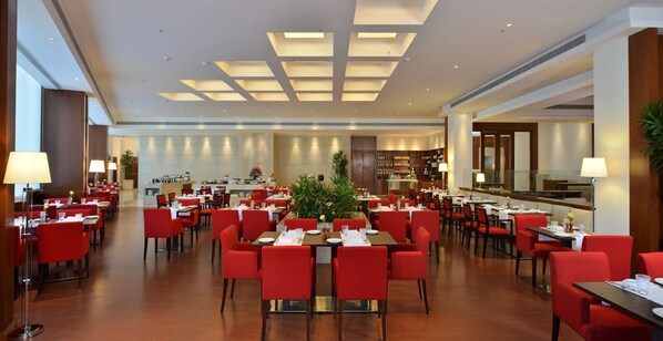 Espaço de refeições de hotel com cadeiras, mesas e uma planta no centro.