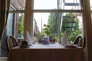Mesa de jantar posta para dois, com vista para um jardim através de uma janela.