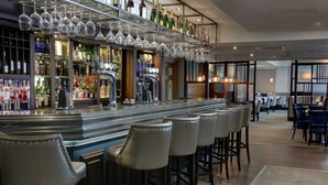 Uma área de bar com um balcão comprido, vários bancos e uma variedade de garrafas e copos.