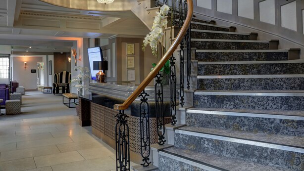 Uma escadaria imponente com design curvo, degraus de mármore e um candelabro.