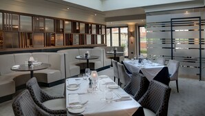 Restaurante moderno com teto alto e claraboia, apresentando uma variedade de assentos, incluindo cabines e mesas, e uma parede decorativa com painéis verticais.