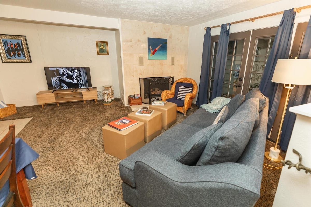 Uma sala de estar com um sofá azul, uma televisão, uma lareira e uma janela com cortinas.