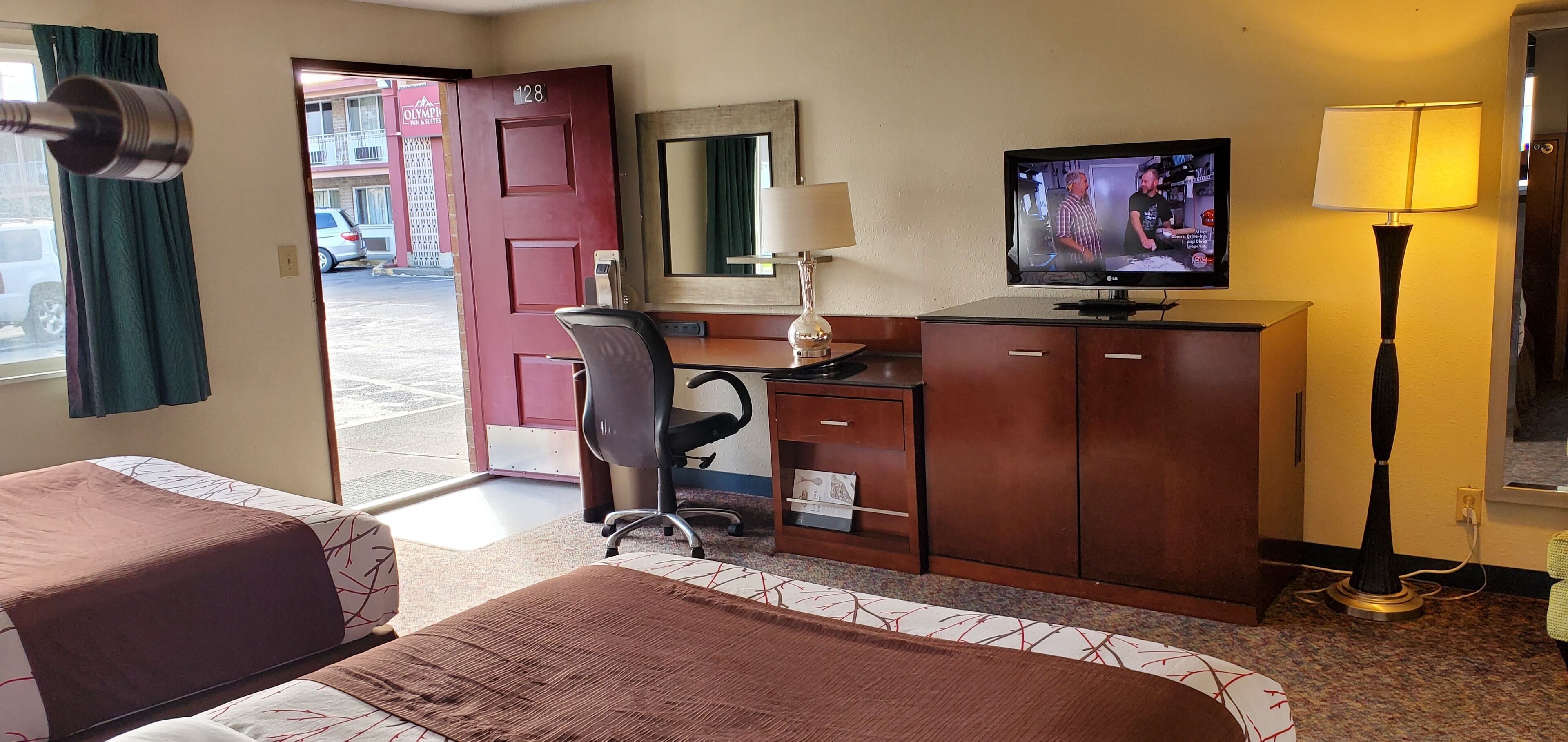 Quarto de hotel com duas camas, uma mesa, televisão e luminária.