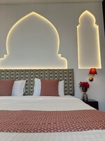 Quarto de hotel com uma cama grande, cabeceira estampada e luminária fixada na parede.