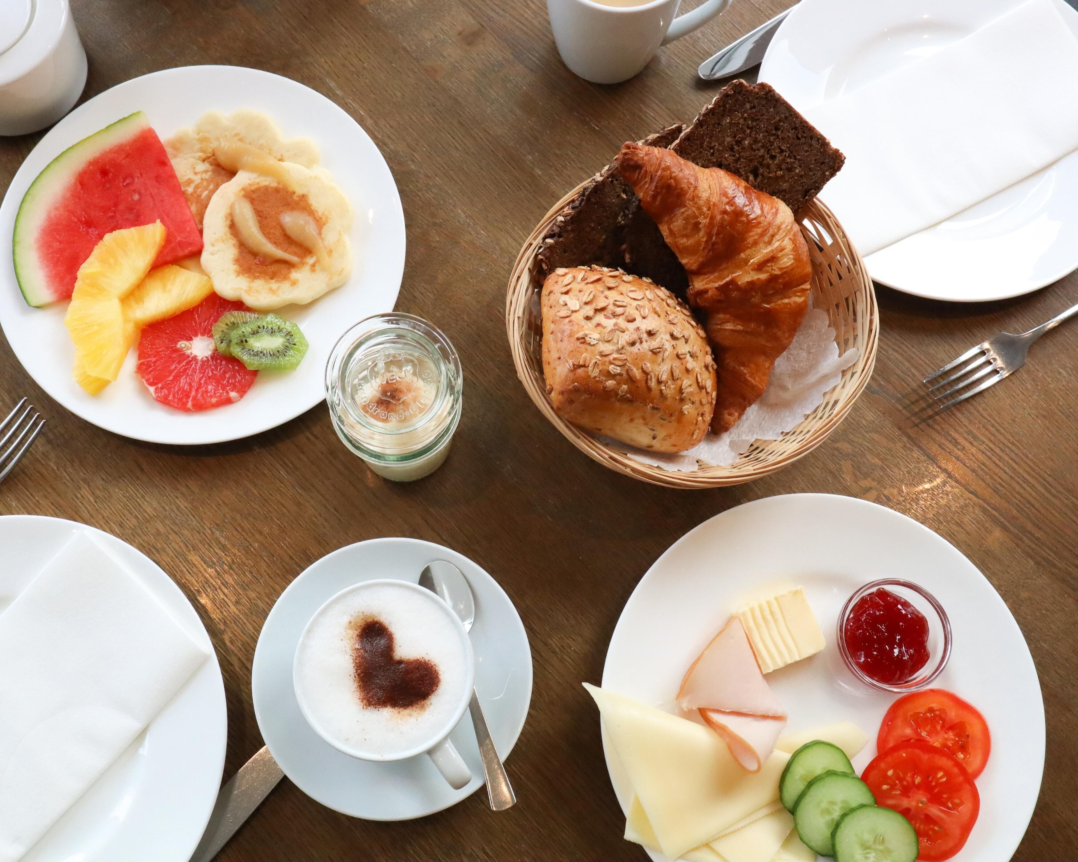 Mesa de café da manhã com frutas, doces, queijo e uma xícara de café.