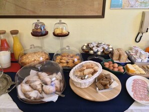 Um buffet de café da manhã com diversos alimentos, incluindo pães, ovos, queijos e doces.