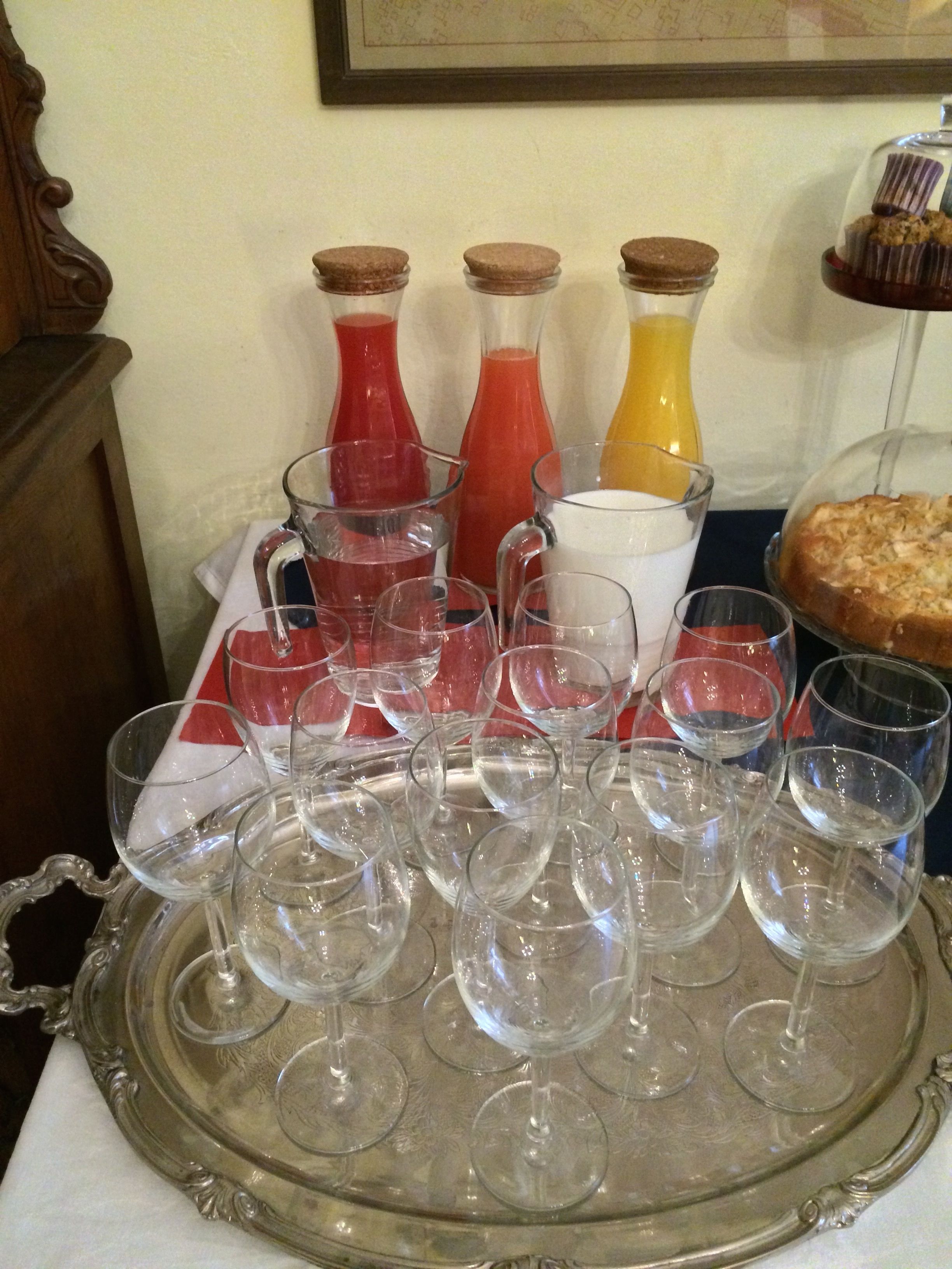 Uma bandeja com vários copos de vinho e três garrafas de suco sobre uma mesa.