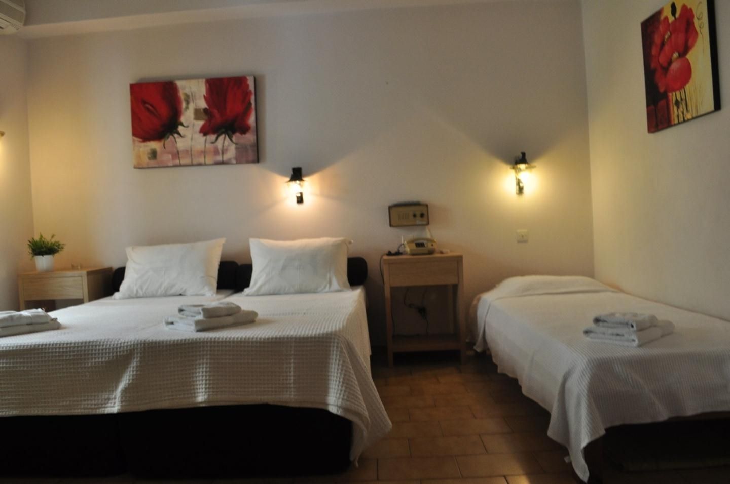 Quarto de hotel com duas camas, uma mesinha de cabeceira com abajur e um rádio fixado na parede.