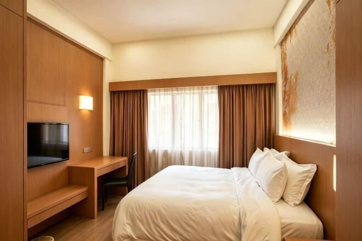 Quarto de hotel com cama, escrivaninha, televisão e janela com cortinas.