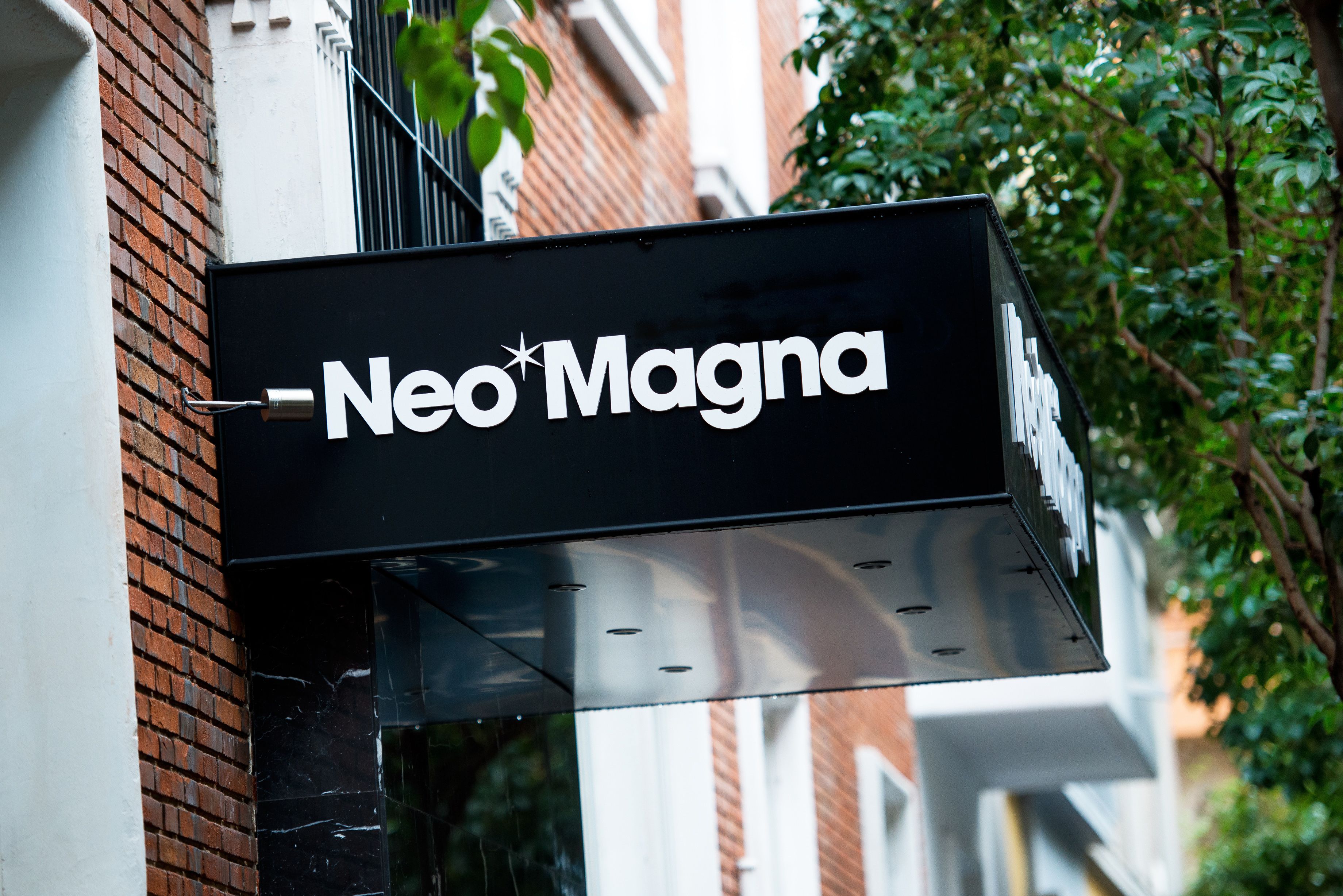 Uma placa preta com texto branco que diz 'Neo Magna' fixada em um edifício.