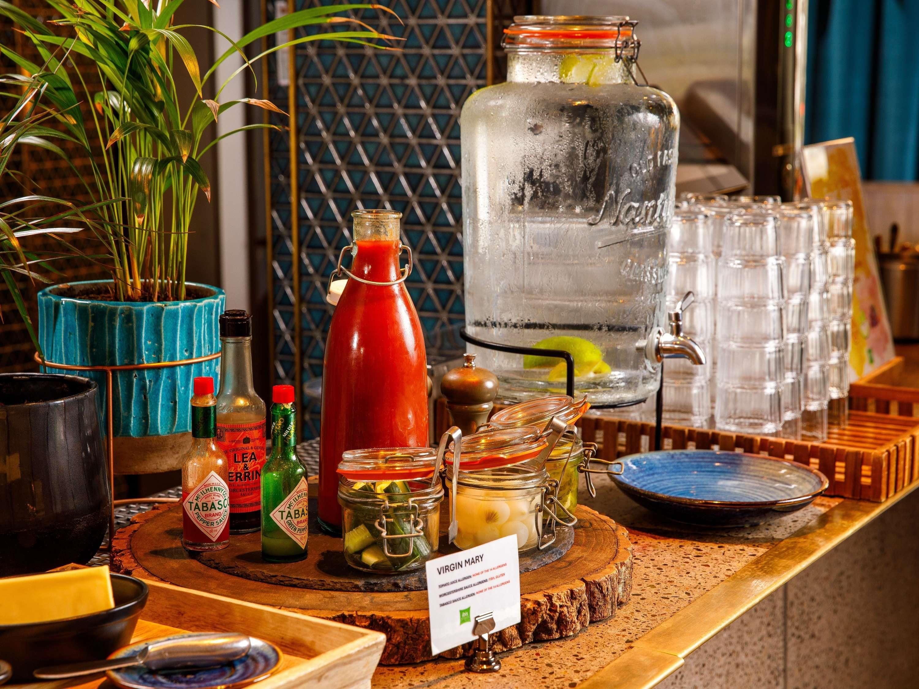 Uma área de bar com diversos temperos, um grande dispensador de água e uma planta em vaso.