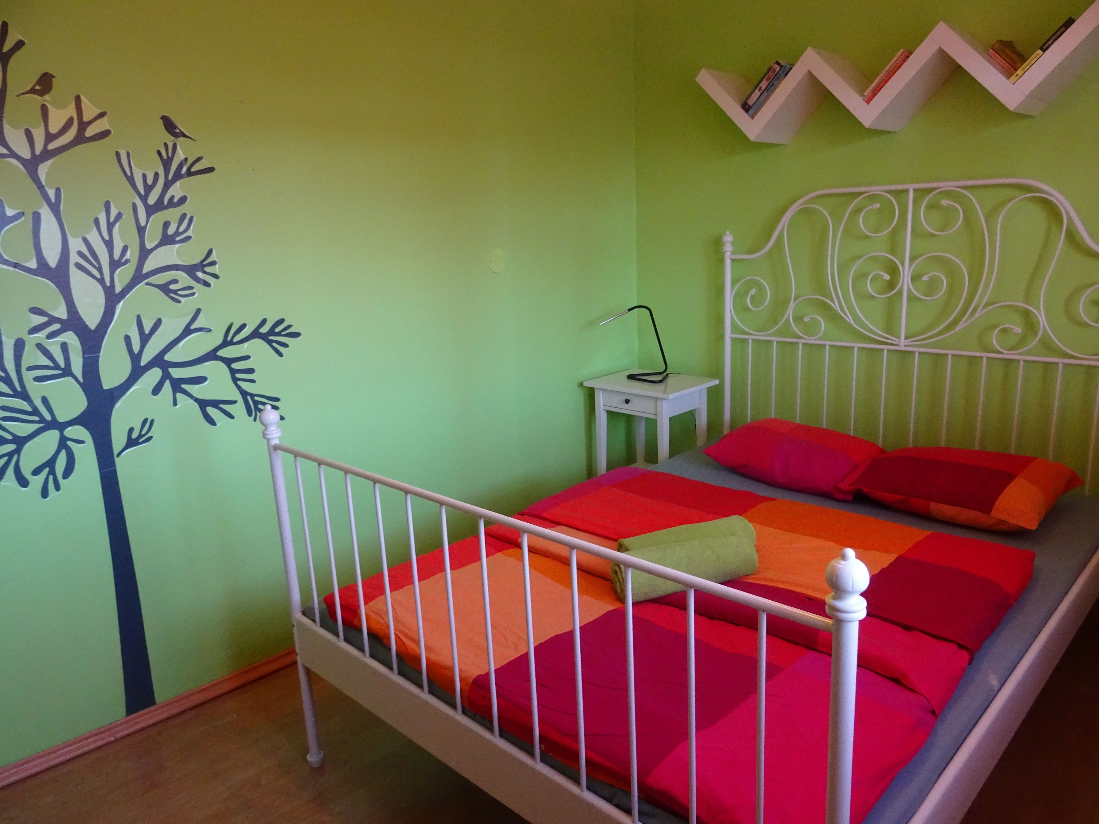Quarto com cama, mesa de cabeceira, decoração na parede e estante com livros.