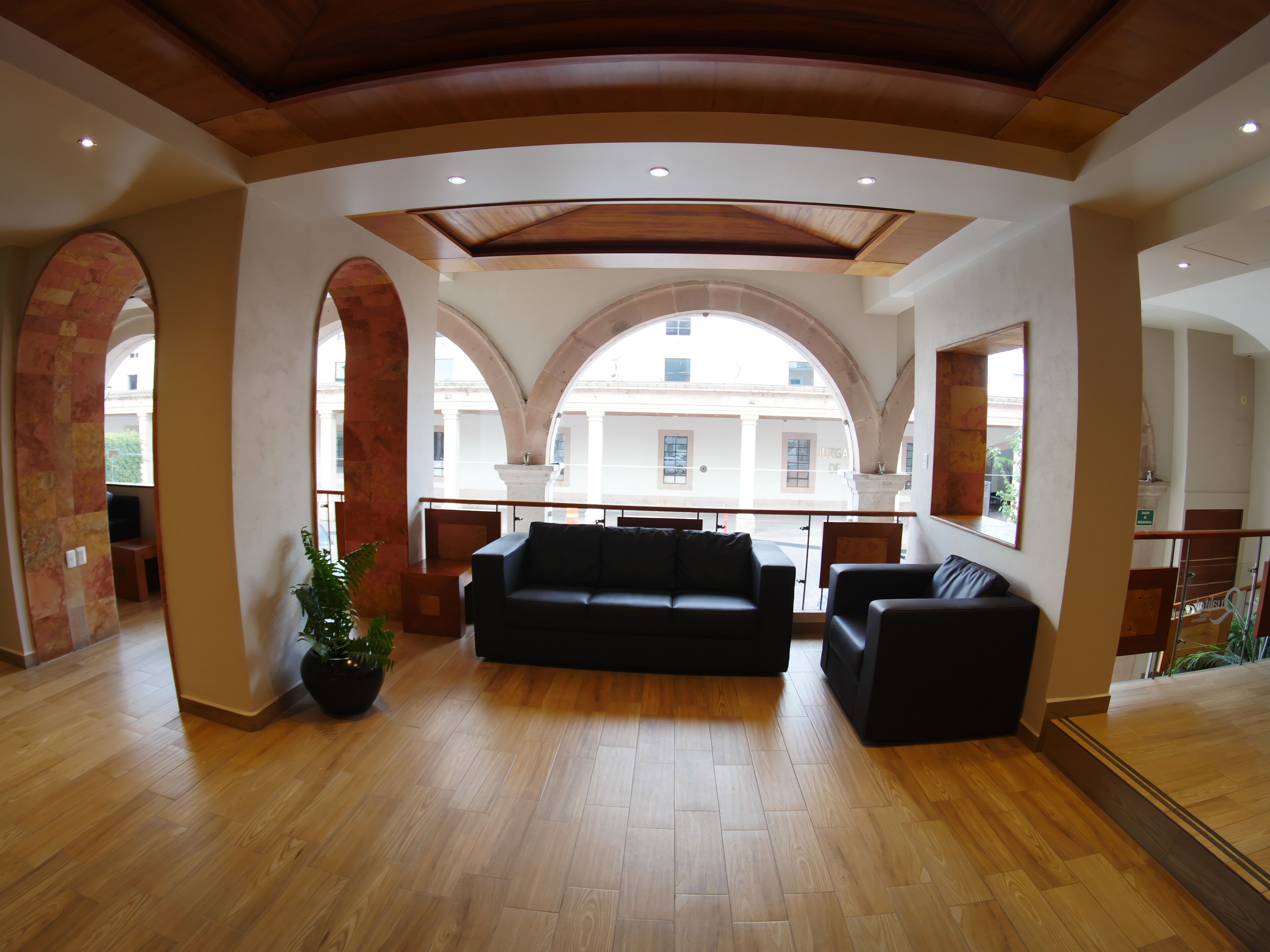 Uma sala de estar espaçosa com piso de madeira, um sofá preto e um vaso de planta.