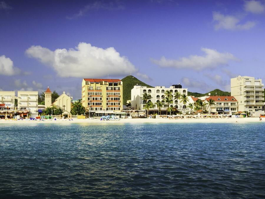 Um hotel à beira-mar com vários edifícios, uma praia e uma montanha ao fundo.