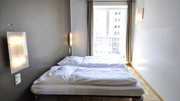 Quarto de hotel com cama, interruptor de luz e vista para um prédio pela janela.