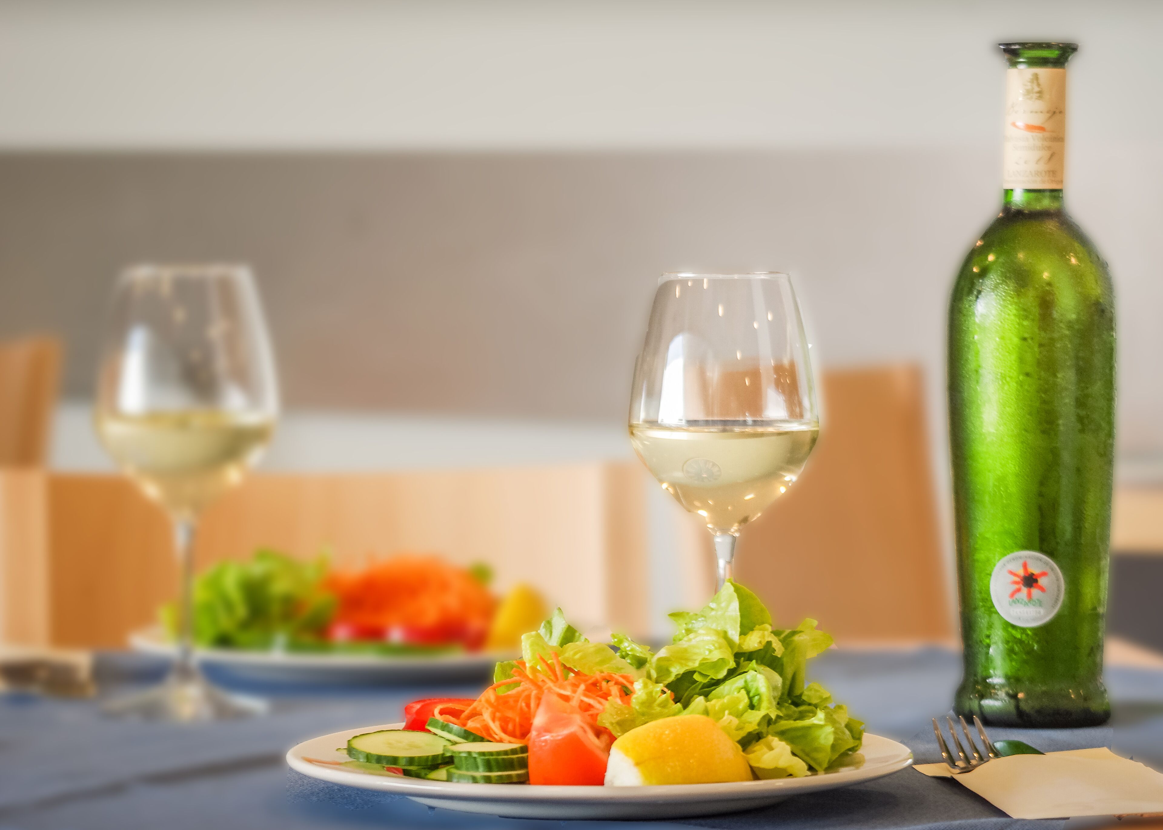 Uma mesa de jantar com uma salada, uma garrafa de vinho branco e dois copos.