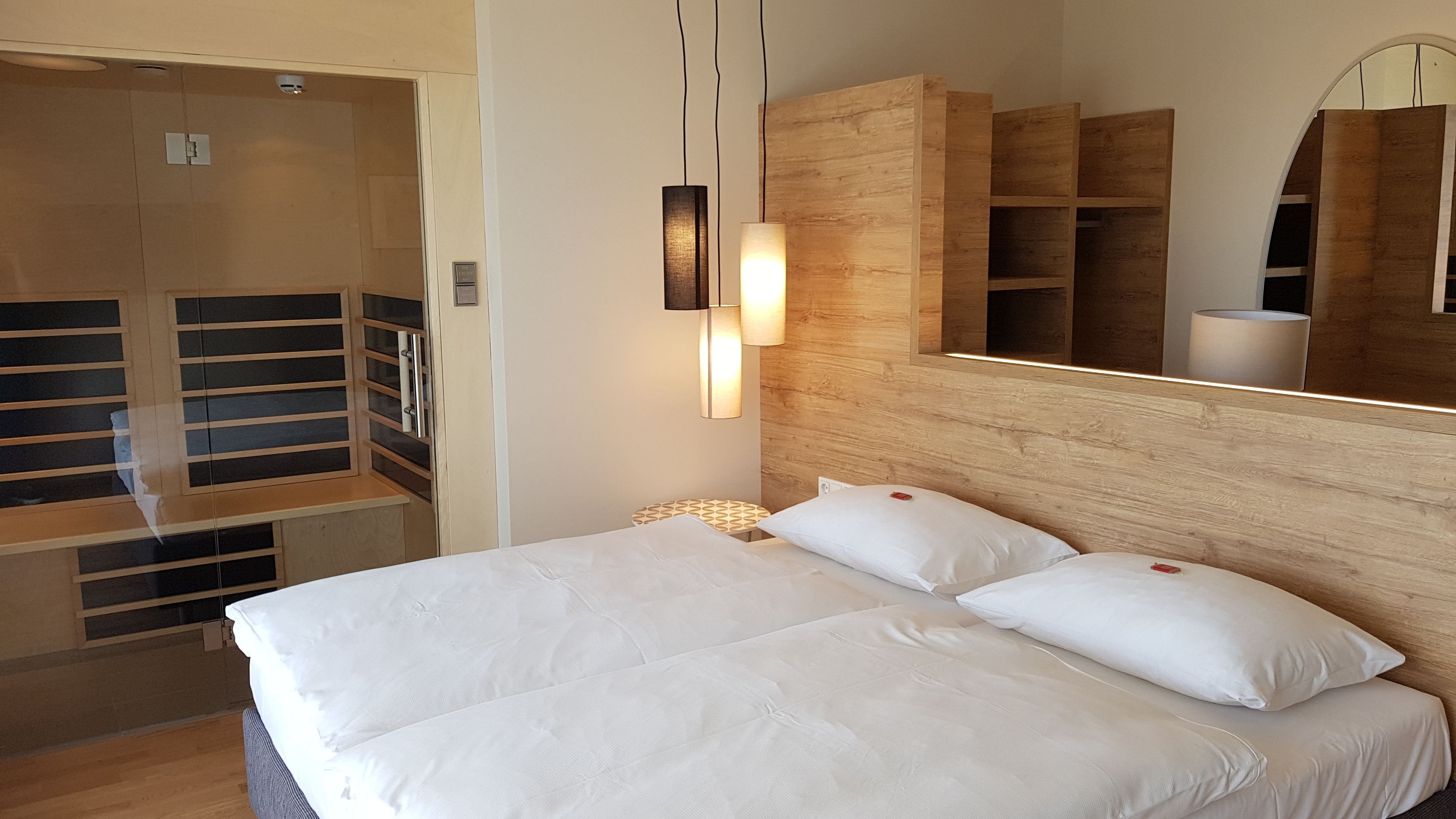 Quarto de hotel com cama grande, cabeceira de madeira, espelho e armário embutido com várias prateleiras.