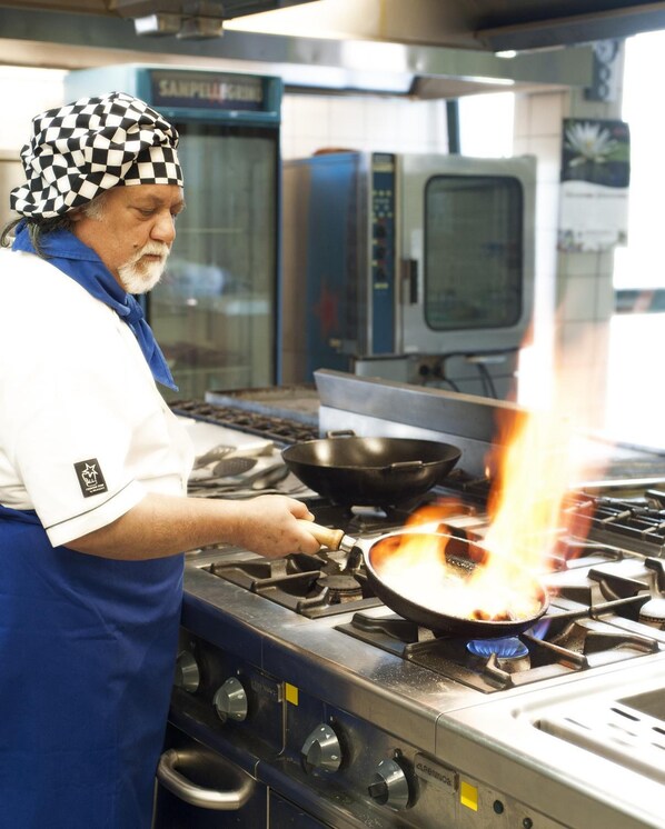 Um cozinheiro preparando comida numa panela sobre um fogão a gás em uma cozinha profissional.