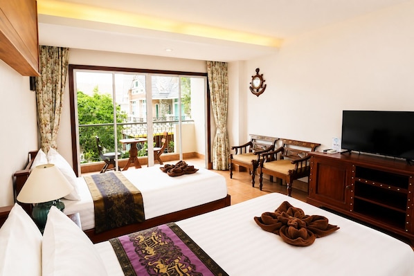 Quarto de hotel com duas camas, televisão, escrivaninha e varanda com vista para edifícios e vegetação.