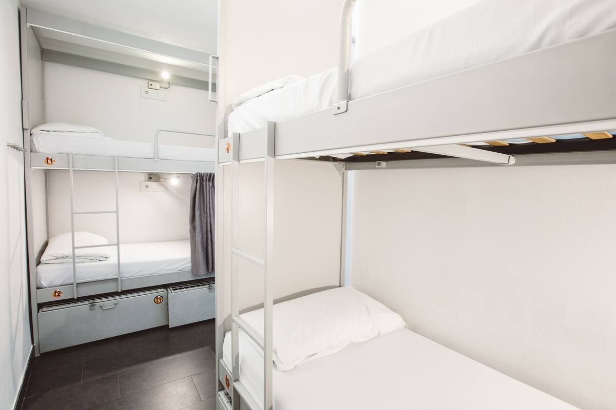 Quarto com beliches, um pequeno guarda-roupa e janela com cortinas.
