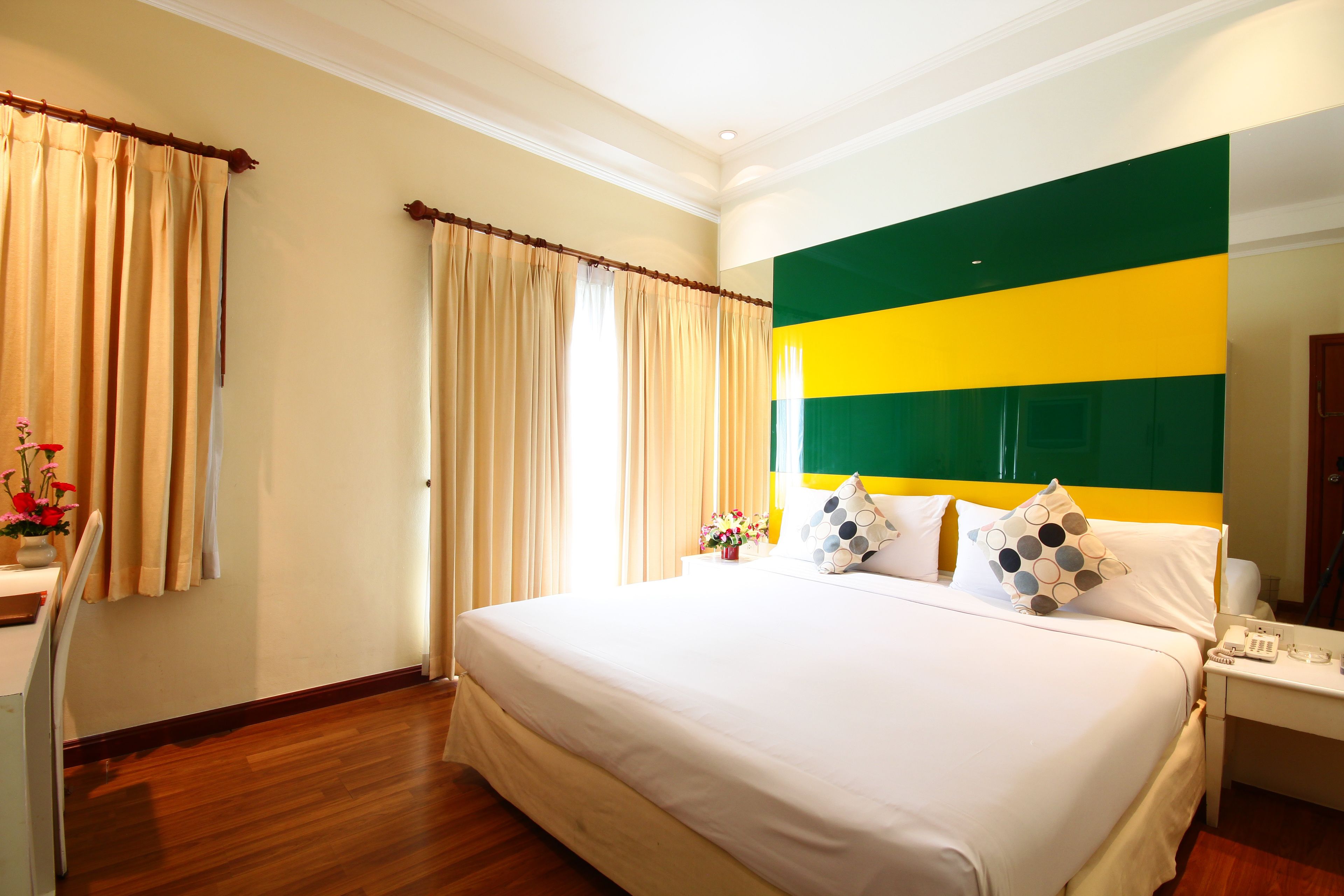 Quarto de hotel com uma cama grande, mesa de cabeceira com telefone e cortinas nas janelas.
