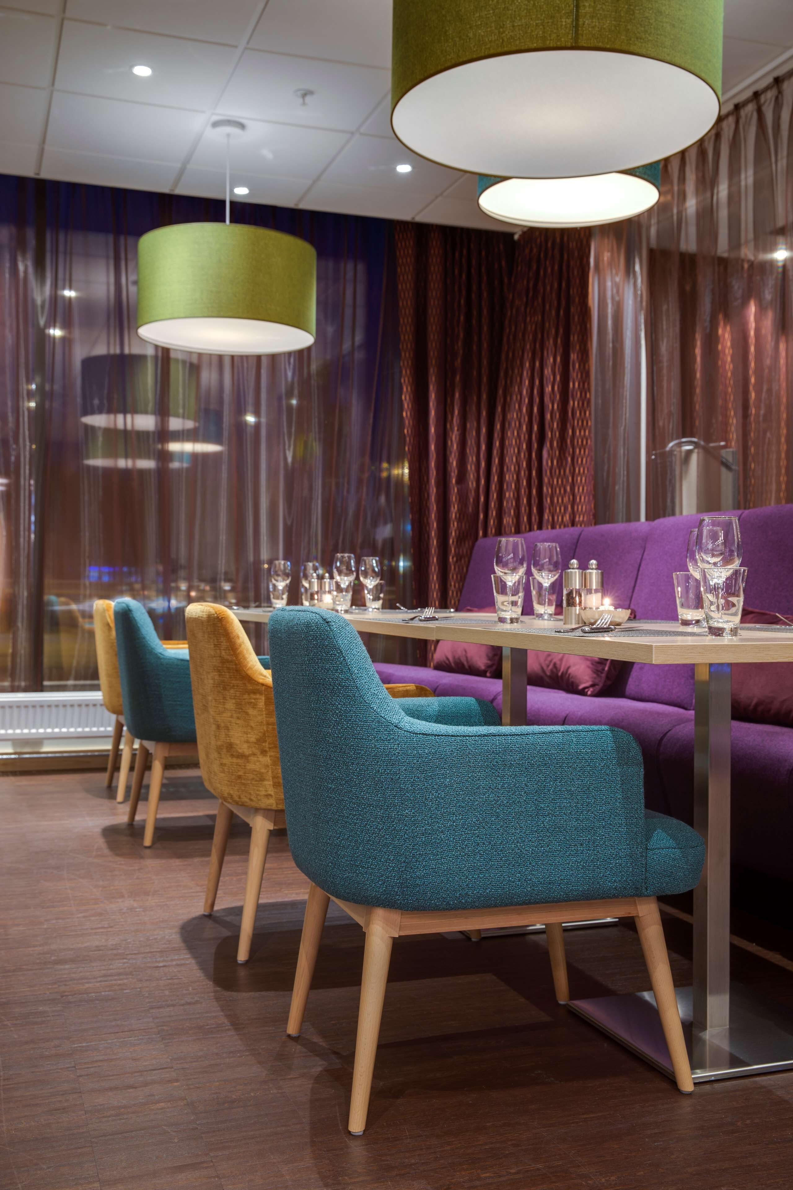 Uma área de refeições moderna com uma mesa posta para dois, um sofá roxo e cadeiras verde-água.
