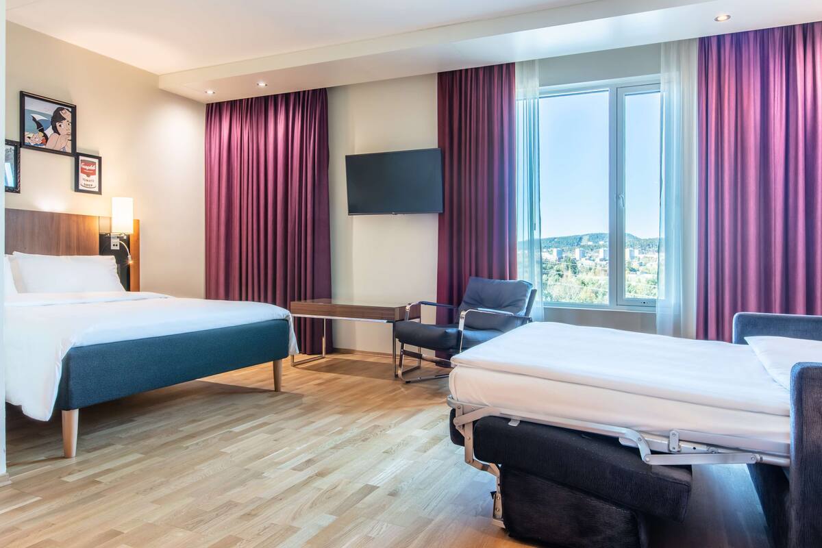 Quarto de hotel com duas camas, televisão, escrivaninha e uma cadeira.